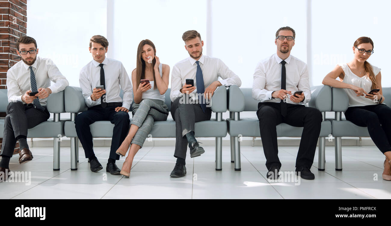 group of young employees sitting in a row in the office waiting room ...