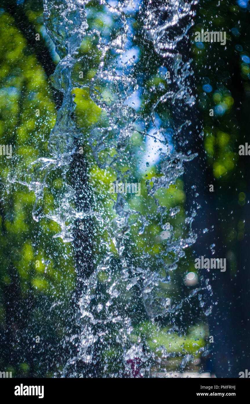 transparent falling water vertical flows against a blue sky and green ...