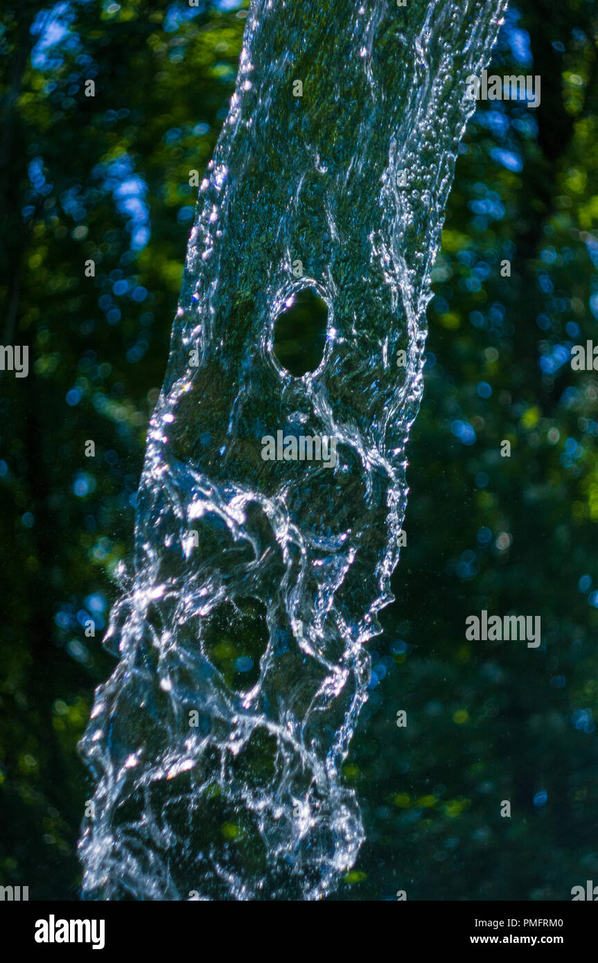 transparent falling water vertical flows against a blue sky and green ...