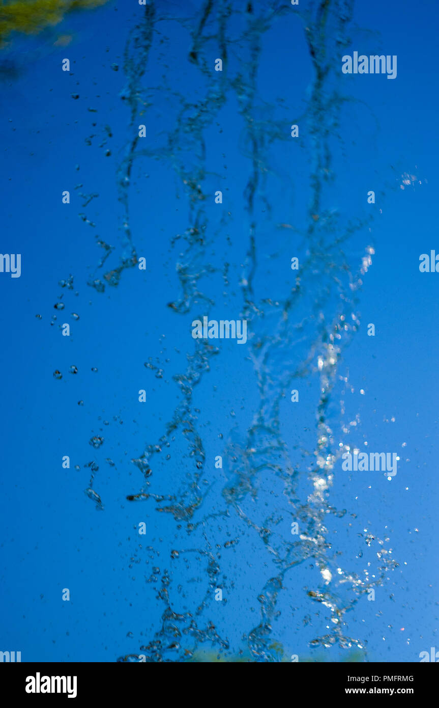 transparent falling water vertical flows against a blue sky and green ...