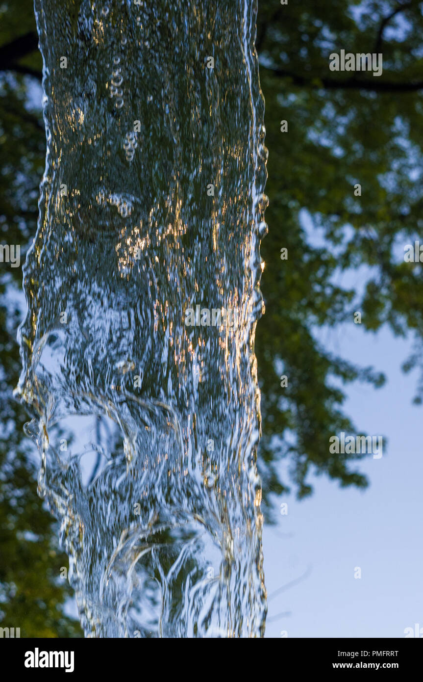 transparent falling water vertical flows against a blue sky and green ...
