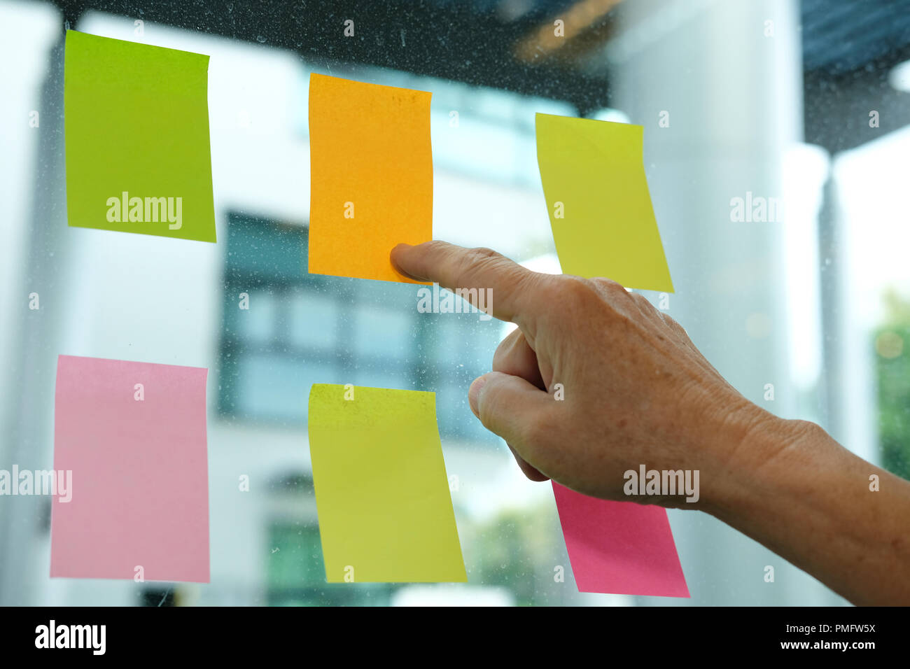 hand pointing at adhesive notes on glass wall at workplace. Sticky note ...