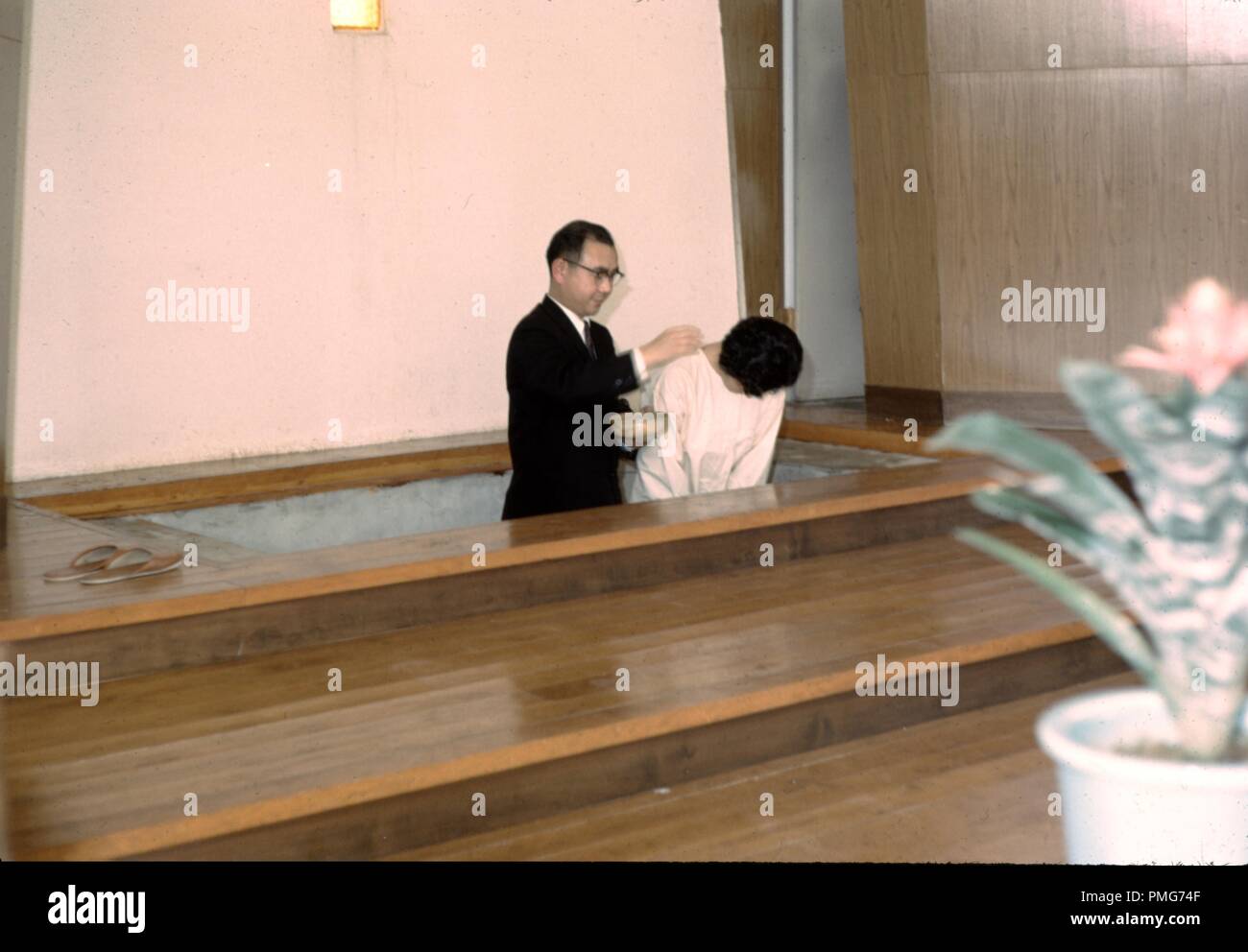 Priest baptizing a Japanese woman, who bows her head, in a Christian ...