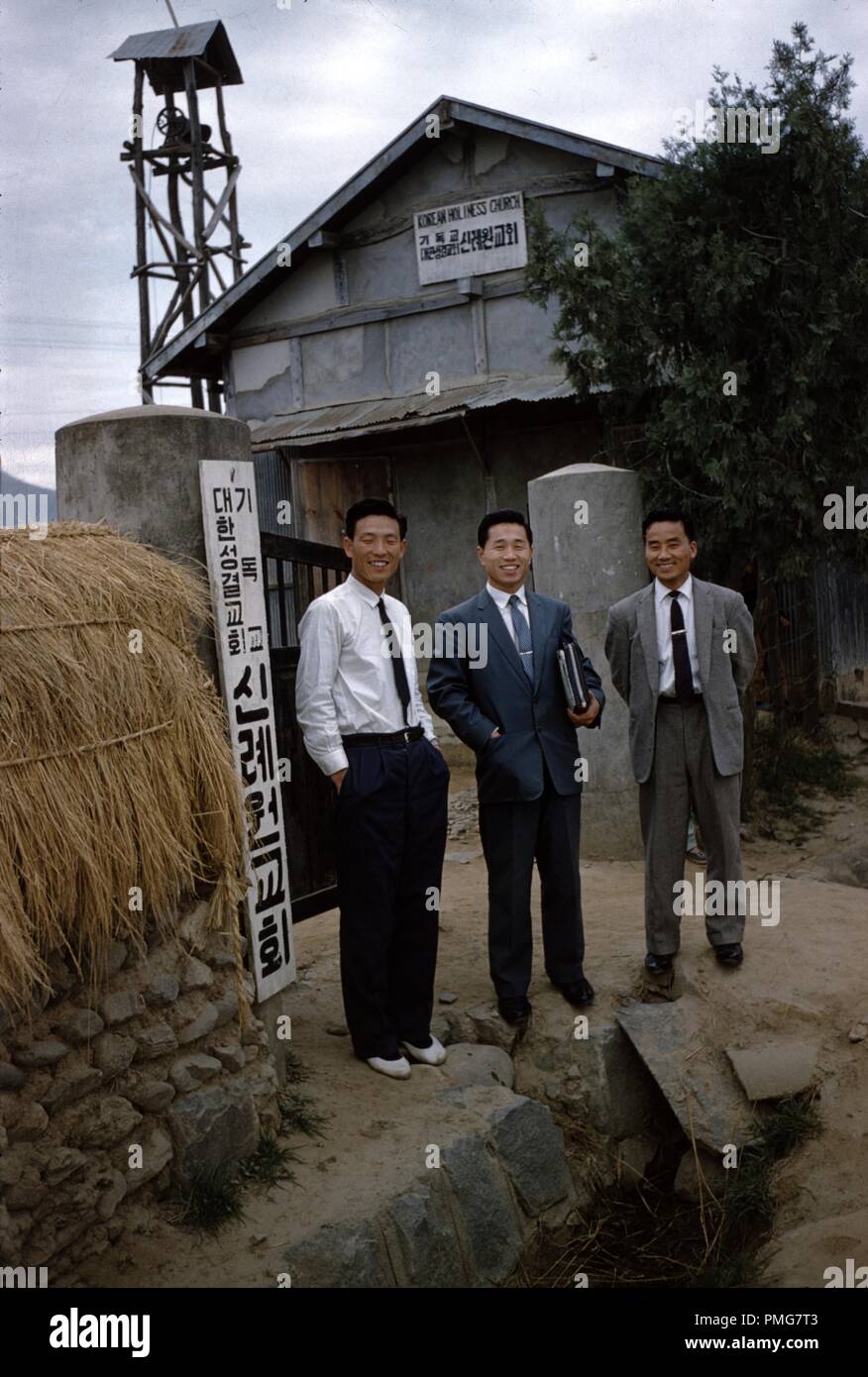 Three men in suits smile and stand together outside the Korean Holiness ...