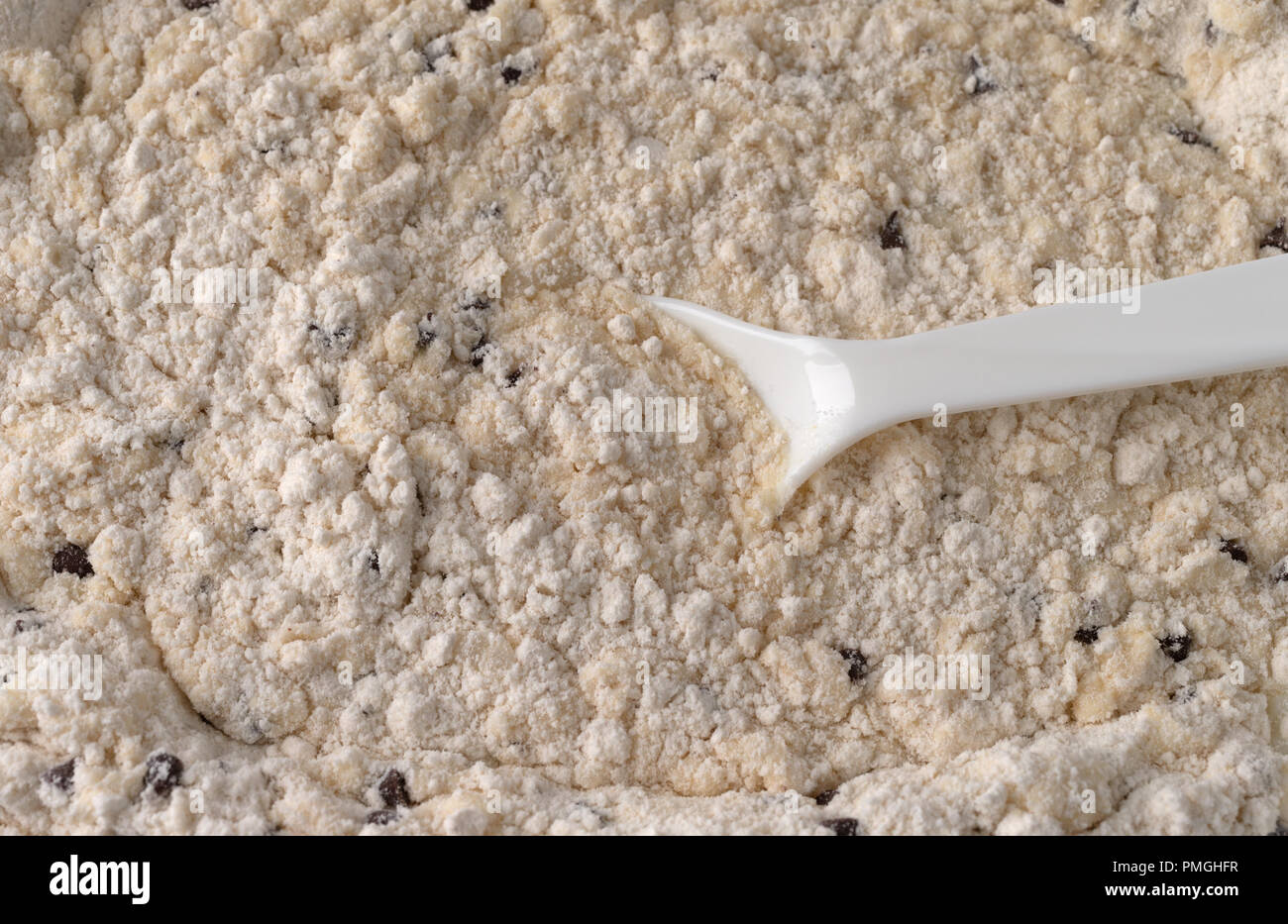 Top view of dry clumpy chocolate chip muffin mix with a white spoon ...