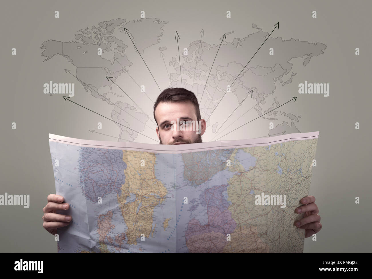 Handsome young man holding a map with world map and arrows behind him ...