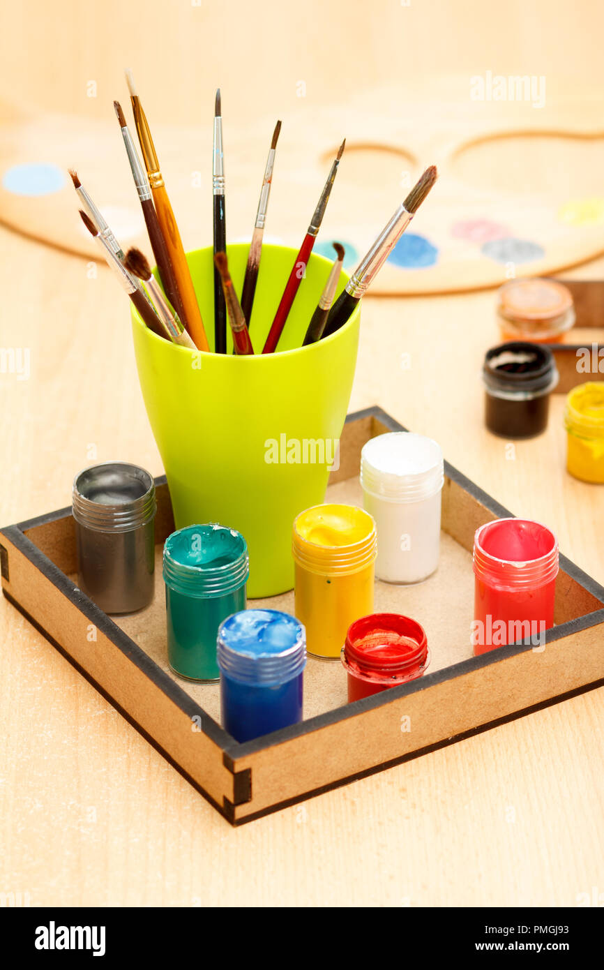 Motley paintbrushes in a cup, palette and paints in box on wooden table ...