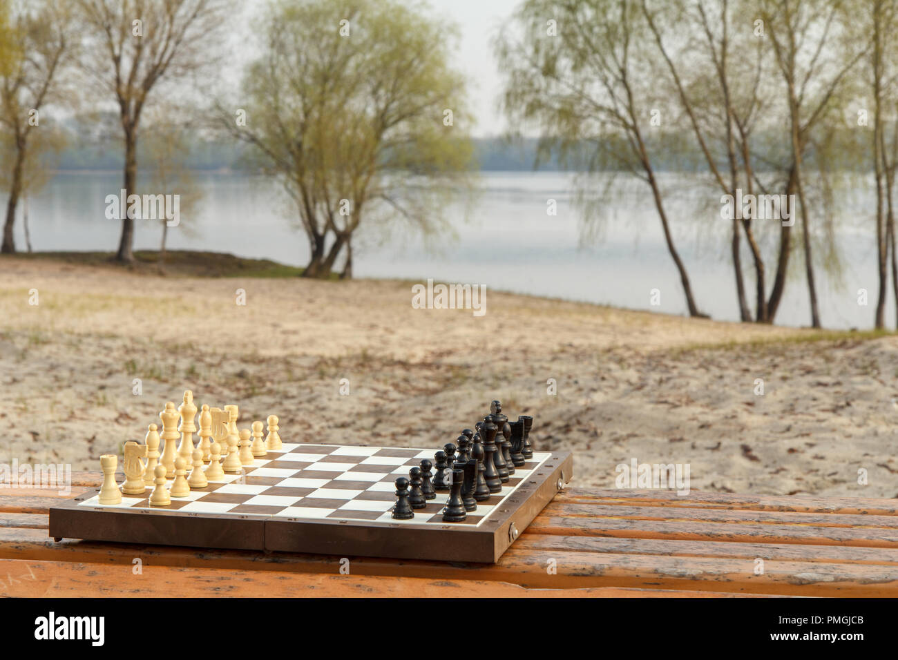 Chess board with chess pieces on wooden bench with river embankment ...