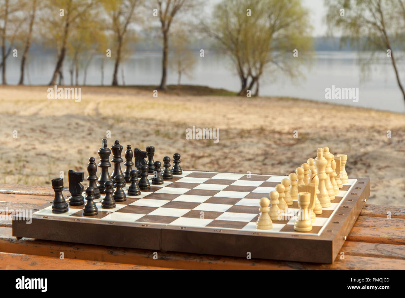 Chess board with chess pieces on wooden bench with river embankment ...