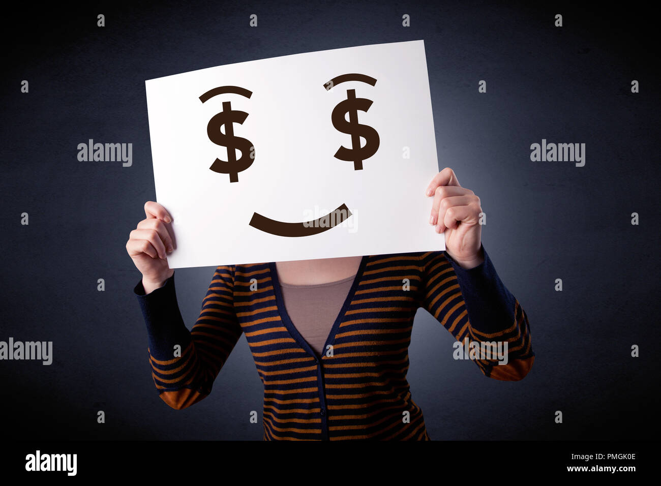 Young casual woman hiding behind a greedy face drawing on cardboard ...