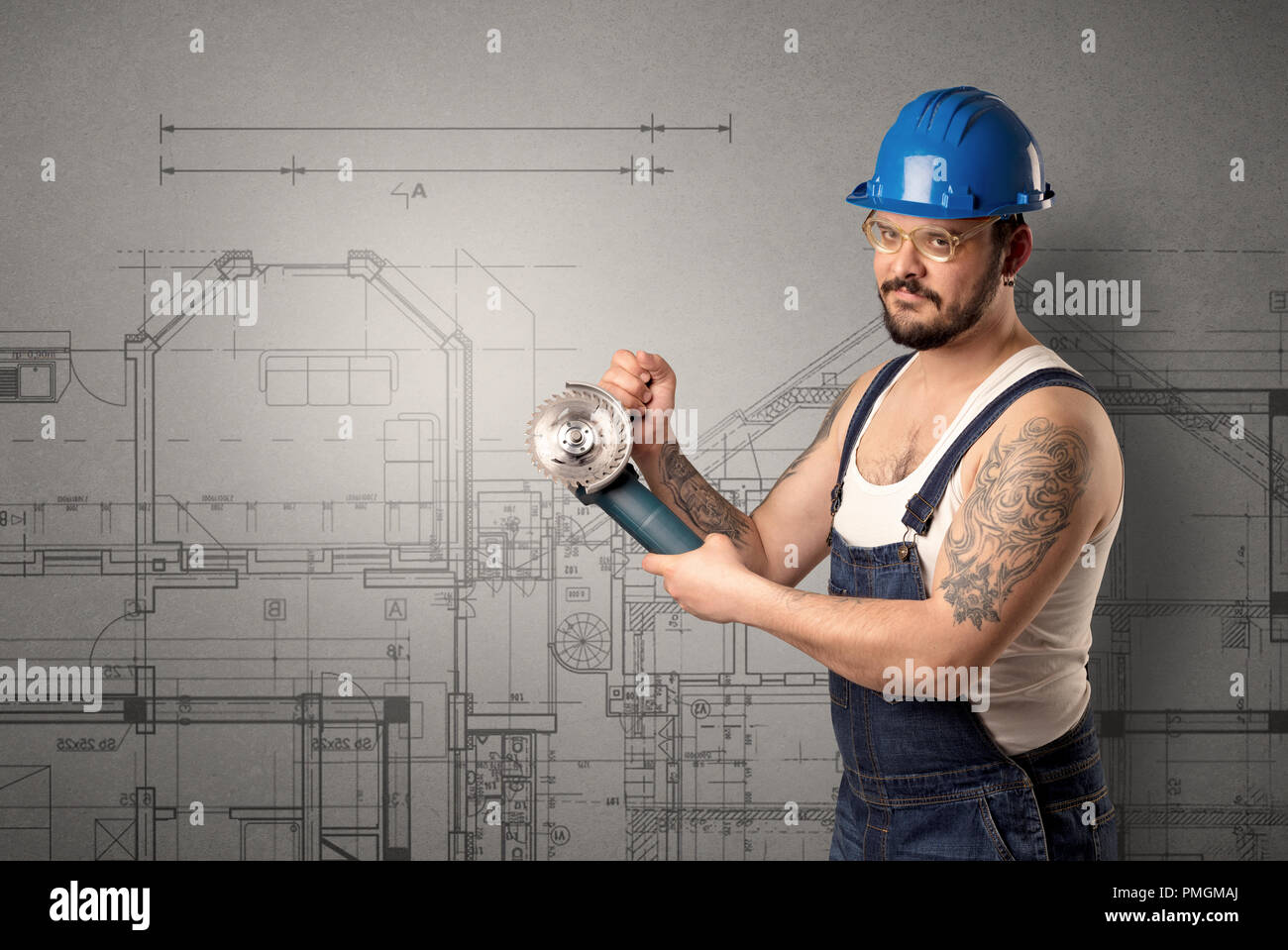 Worker standing with tool in his hand in front of technical drawings ...