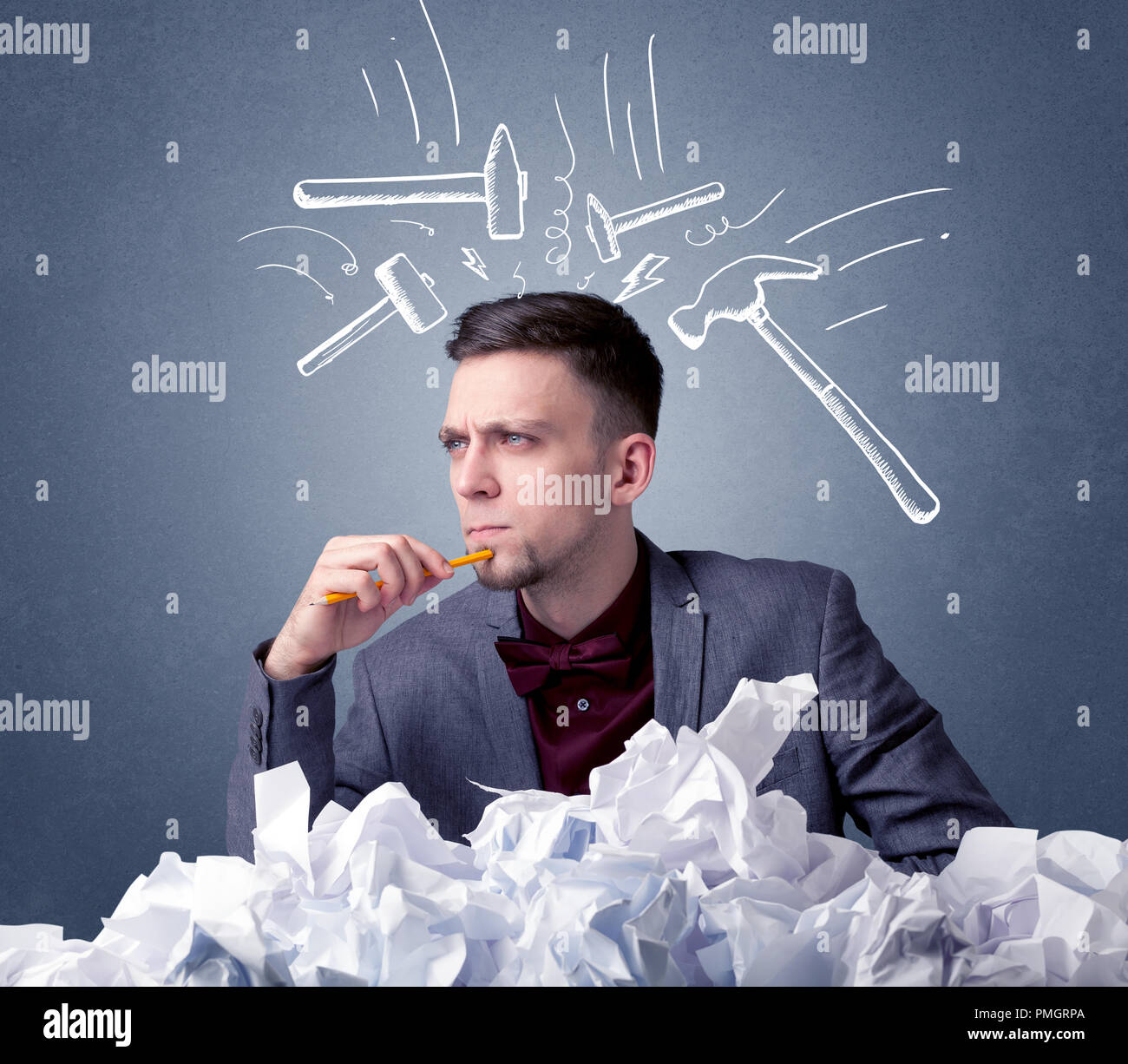 Young businessman sitting behind crumpled paper with drawn hammers ...
