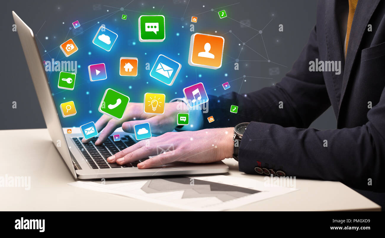 Businessman hand typing on laptop with flying application icons around ...