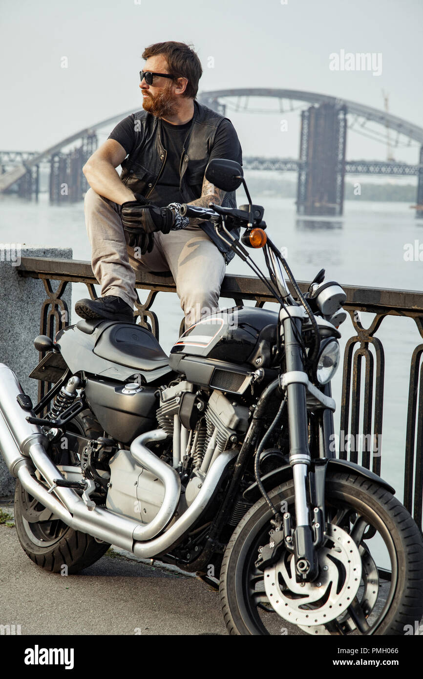 Redhead biker with beard in leather jacket sitting on railings near ...