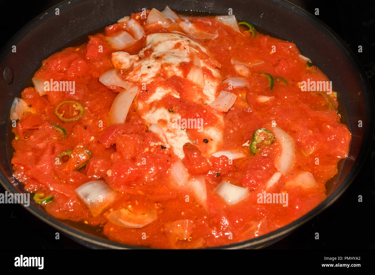 Cooking in a frying pan on a hob, a piece of chicken and some ...