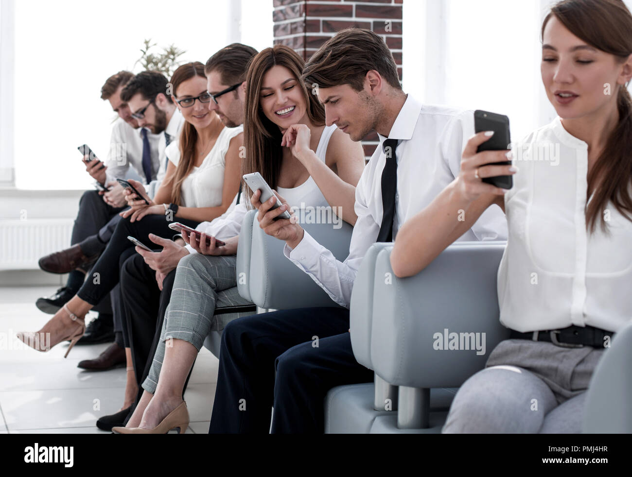 group of employees using their gadgets sitting in the office hallway ...