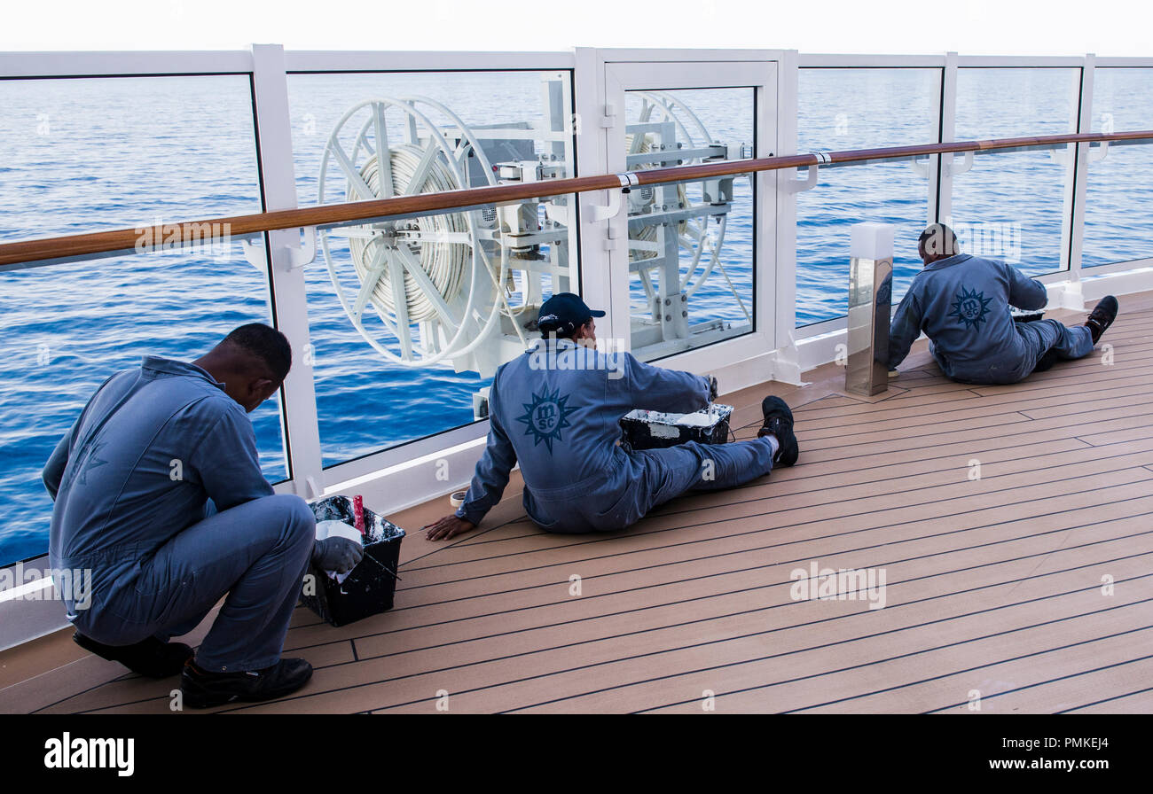 Three crew members, painting metalwork, on cruise ship MSC Seaview ...