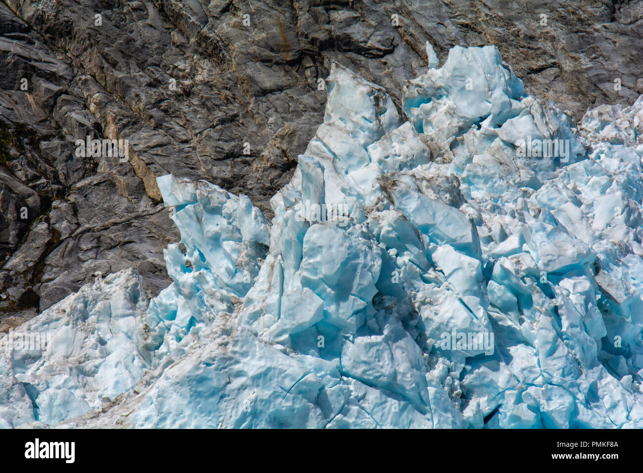 Pale blue glacial ice is pushed up against a grey granite wall Stock ...
