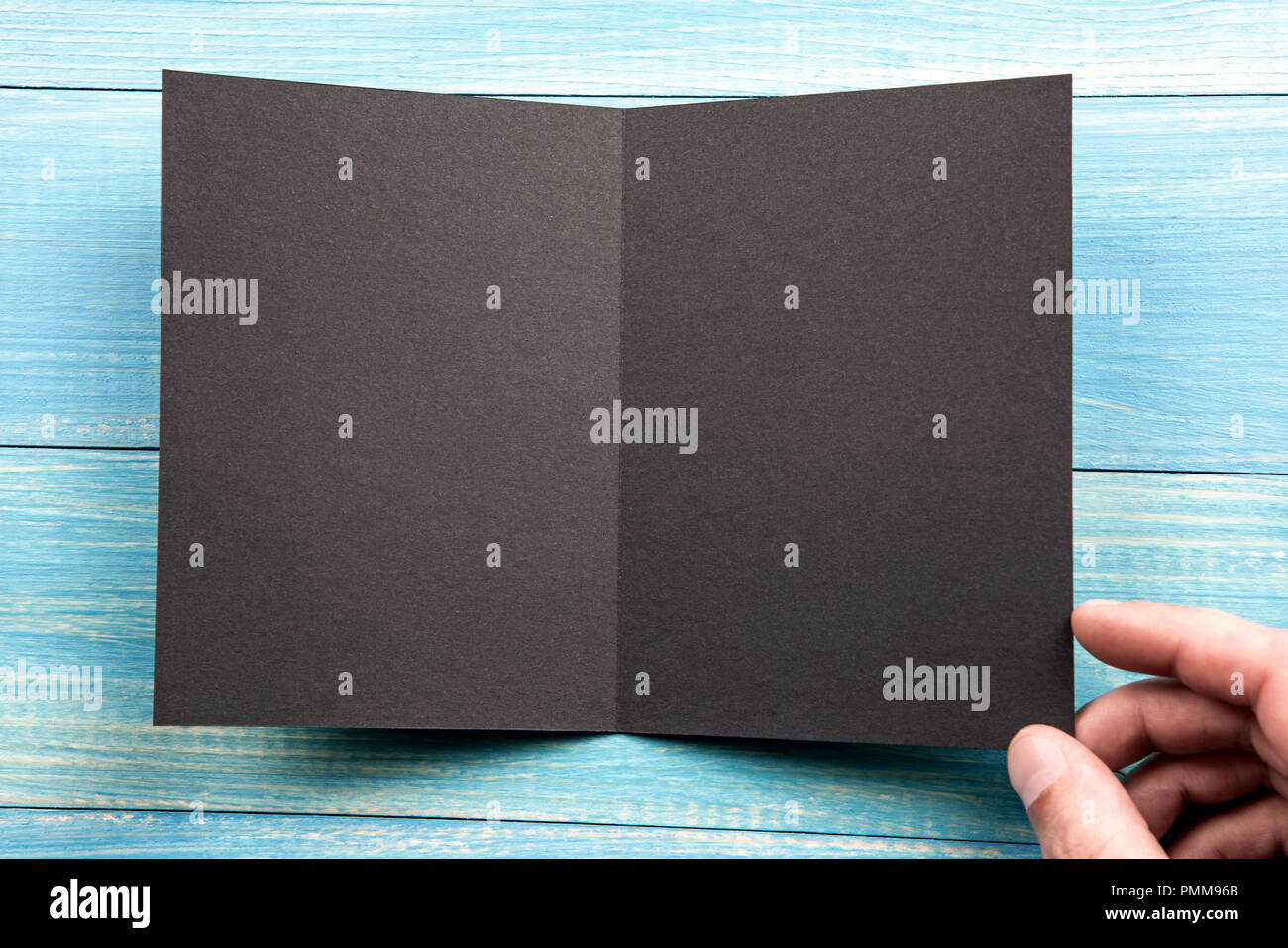 Mens hand holding empty black booklet on blue wooden background. View ...