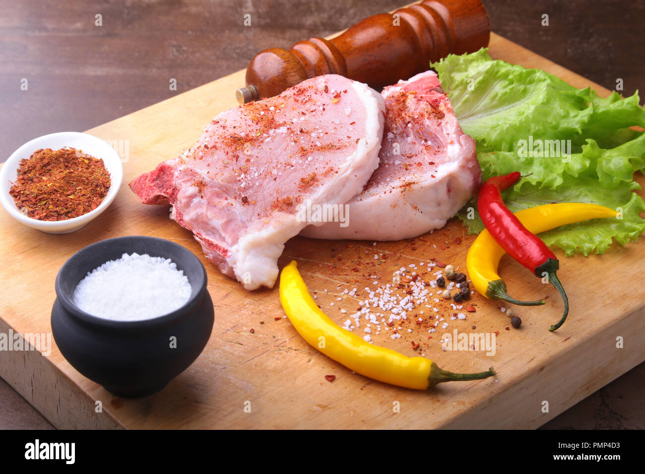 Raw chop on a rustic cutting board with salt, pepper and grinder for ...