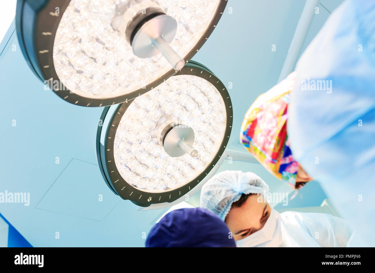 A female surgeons stands under an surgical lamp in operation room while ...