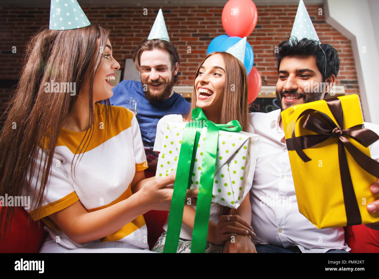 Friends offering gifts to amazing woman in a party hat, they are ...