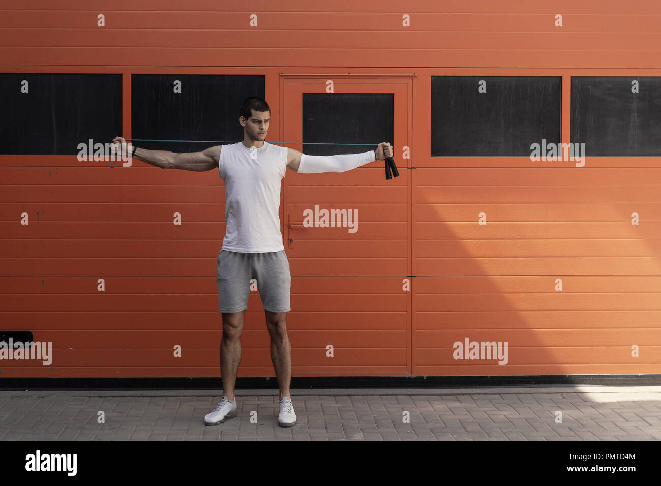 Portrait of muscular young man exercising with jumping rope on orange ...