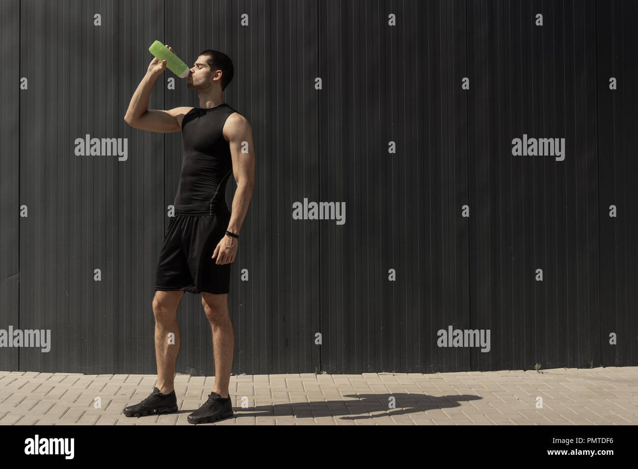 Sport model man drinking water from a plastic bottle on gray background ...
