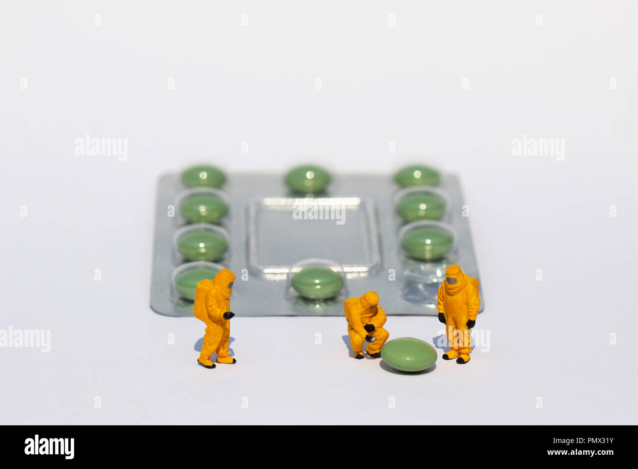 Small scientists in clean suits examining green pill from blister pack ...