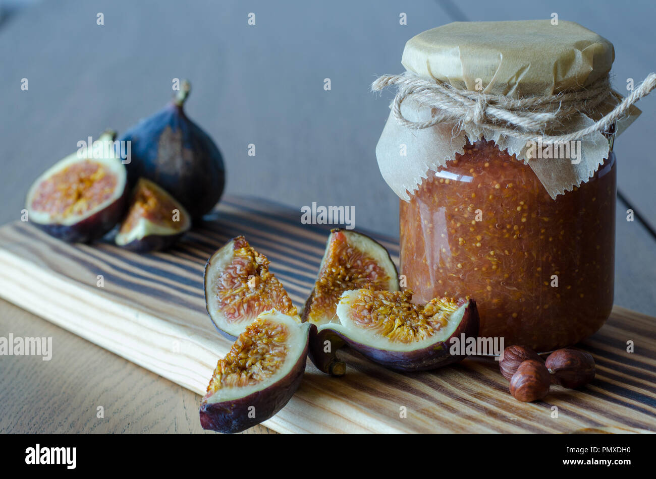Closed glass jar of Fig jam, nuts and sliced figs on a wooden table ...