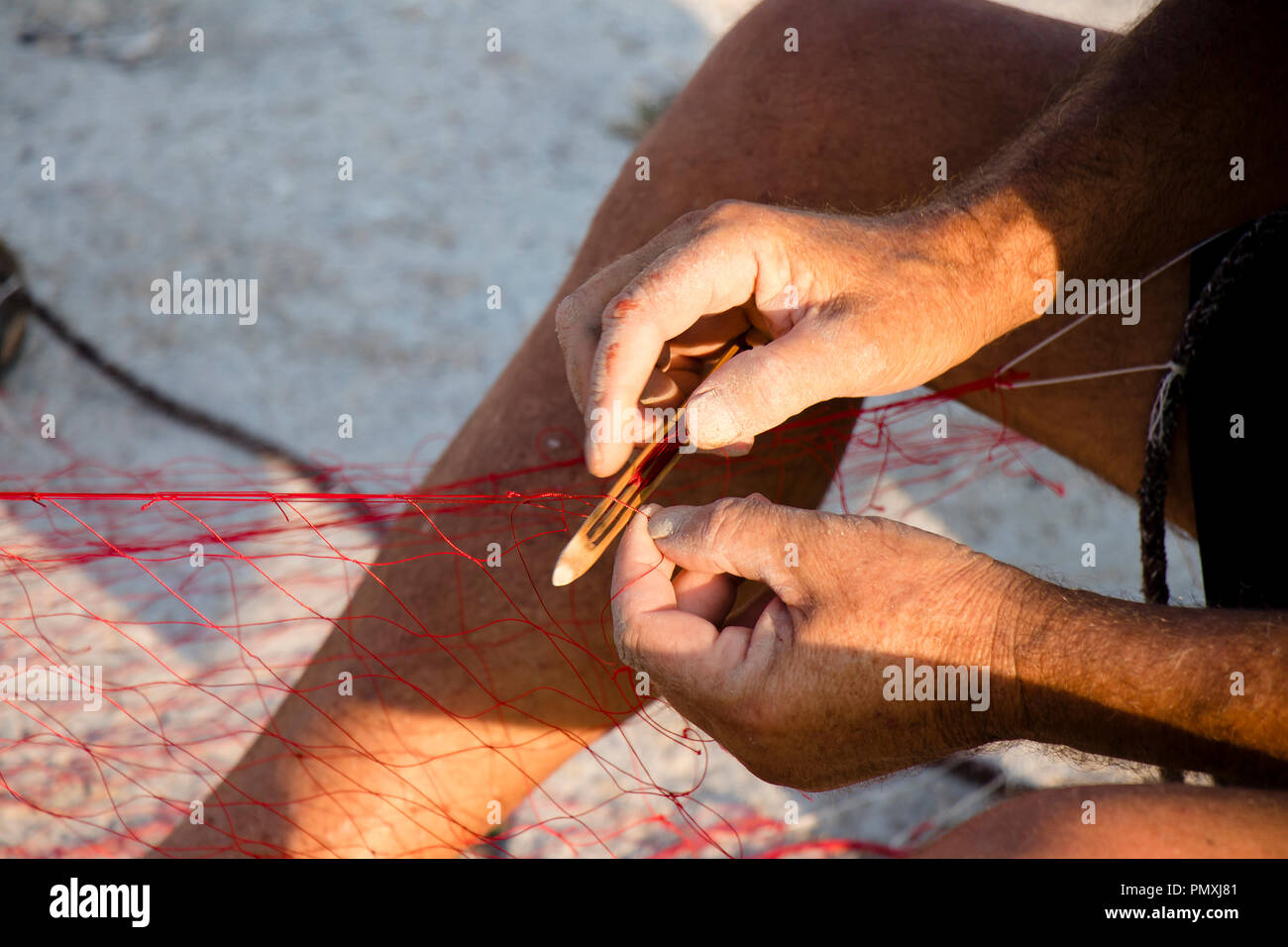 Fisherman hands repairing his red fishing net with needle , close up ...