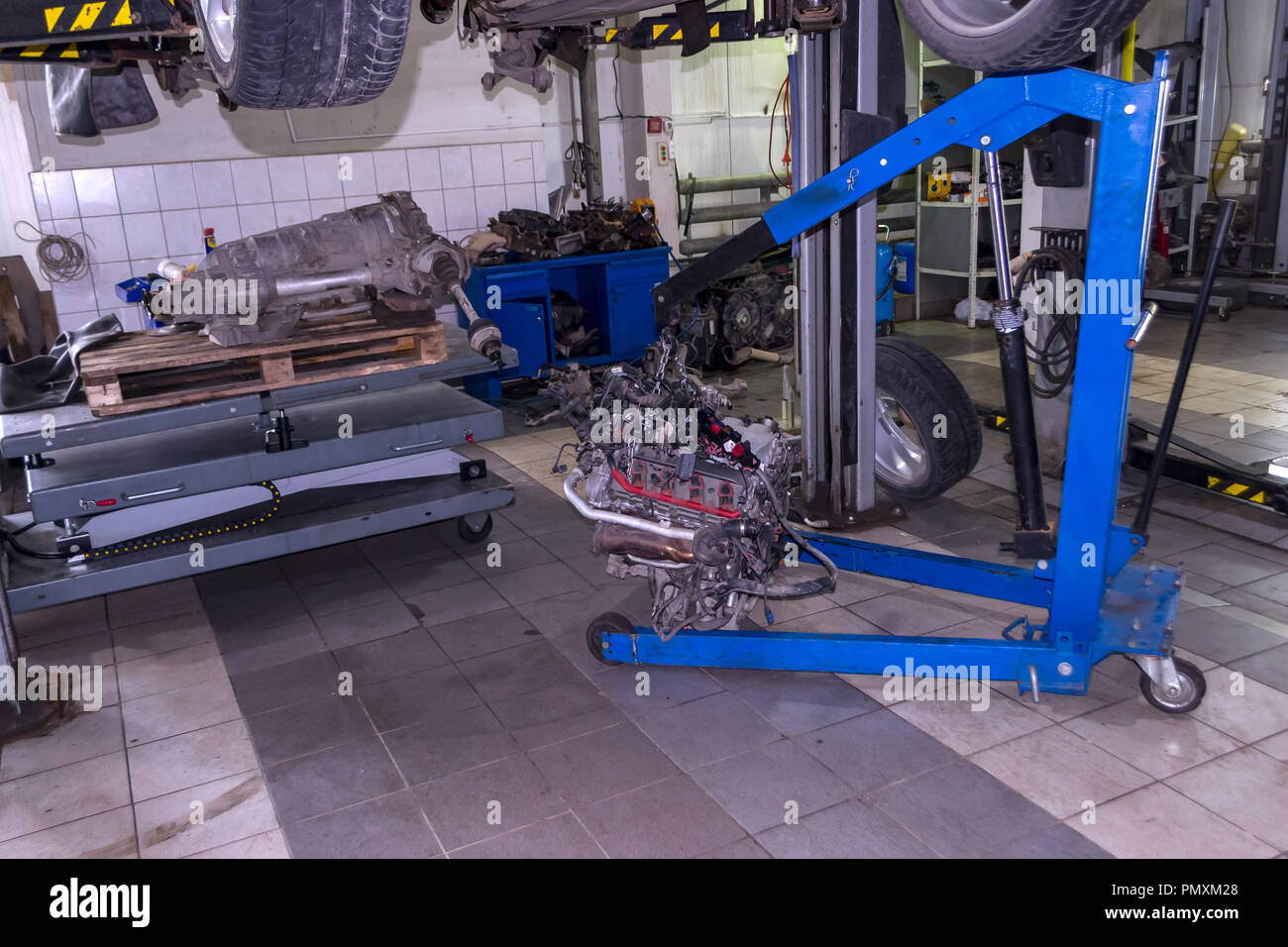A sports car raised on a lift for repair and under it a detached engine ...