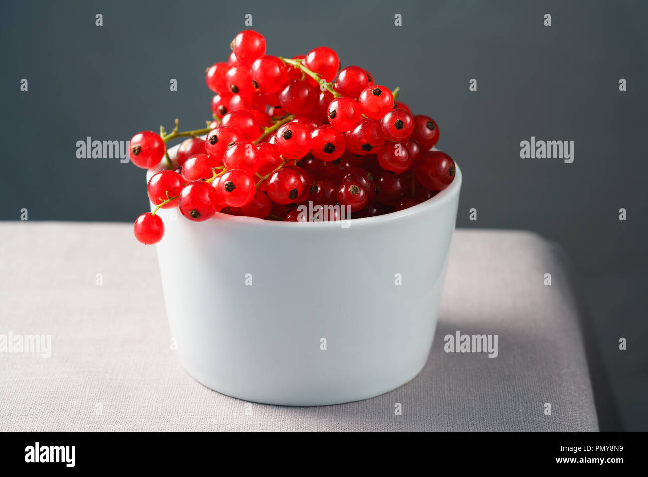 Red currants in a white porcelain bowl. Gray linen table, high ...