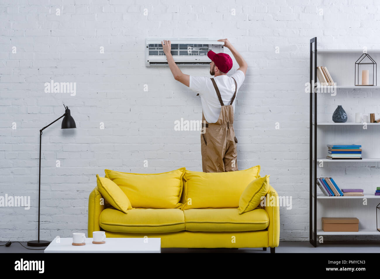 young professional repairman fixing air conditioner hanging on white ...