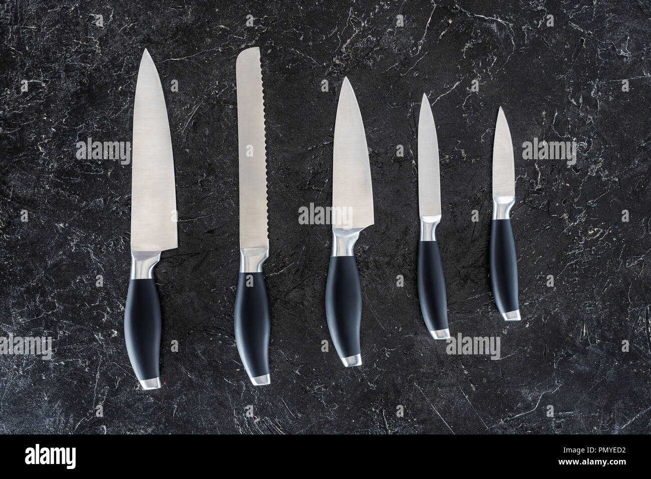 top view of different kitchen knives arranged on black marble surface ...
