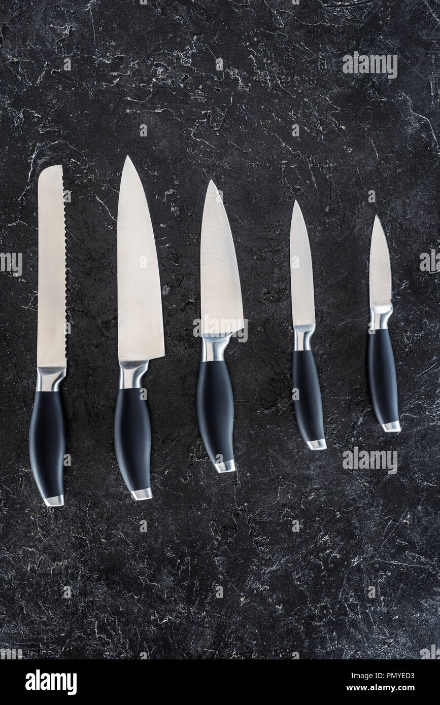 top view of various kitchen knives arranged on black marble surface ...