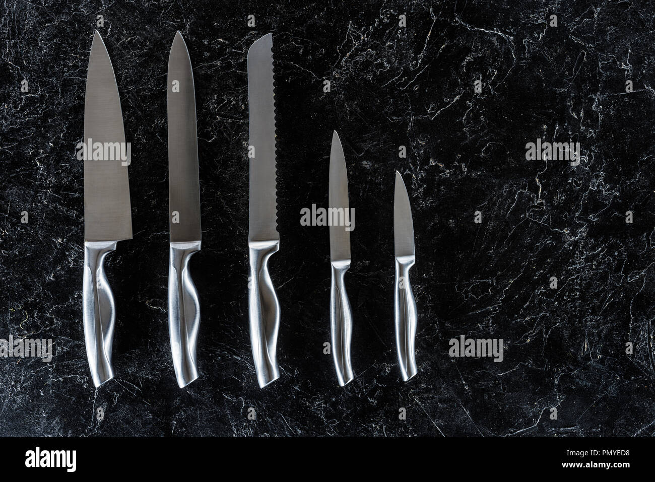 top view of different kitchen knives arranged on black marble surface ...