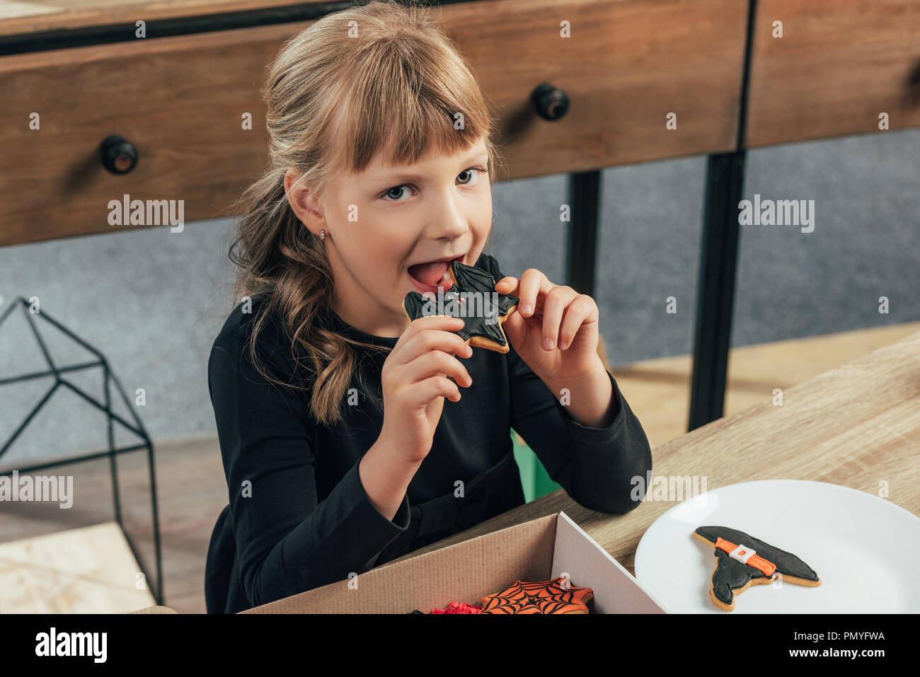 cute child eating halloween cookie and looking at camera at home Stock ...