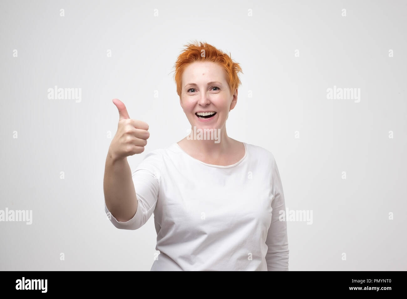 Mature happy cheerful woman with red hair showing thumb up. Number one ...