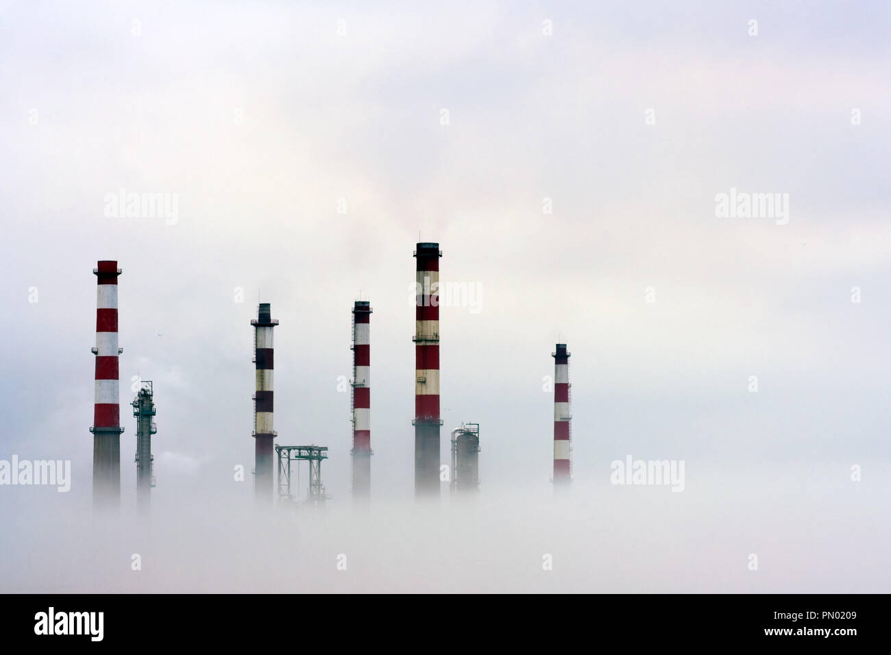 Chimneys of an oil refinery semi losted in the fog Stock Photo - Alamy