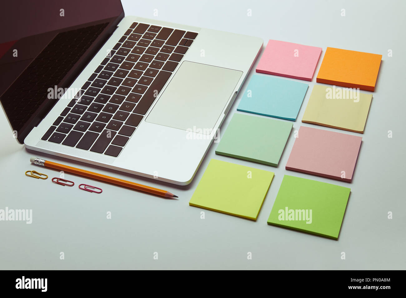 laptop, set of colored paper stickers, pencil and paper clips on white ...