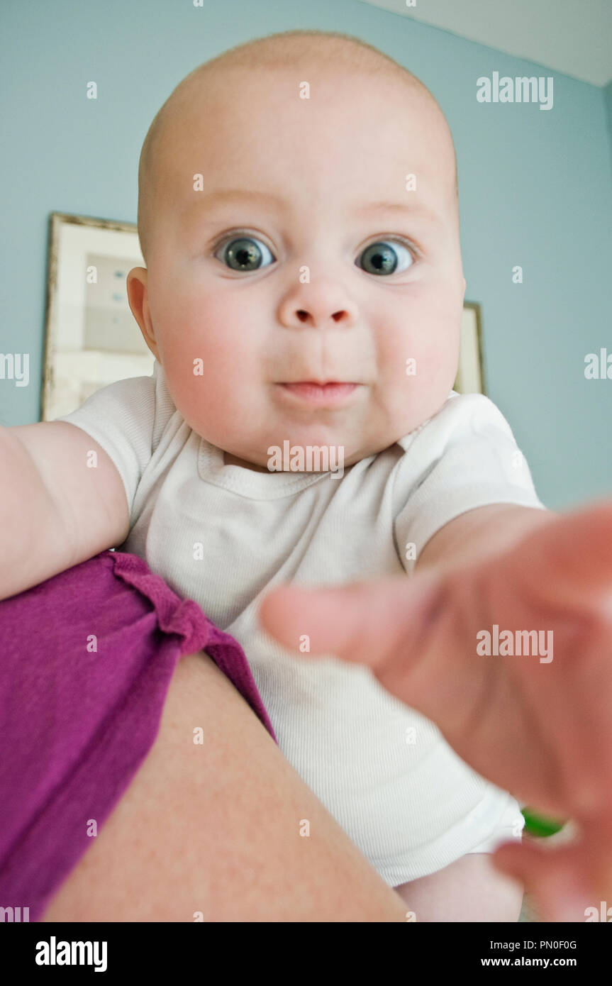 A six month old baby being held by her mother grabbing at the camera ...