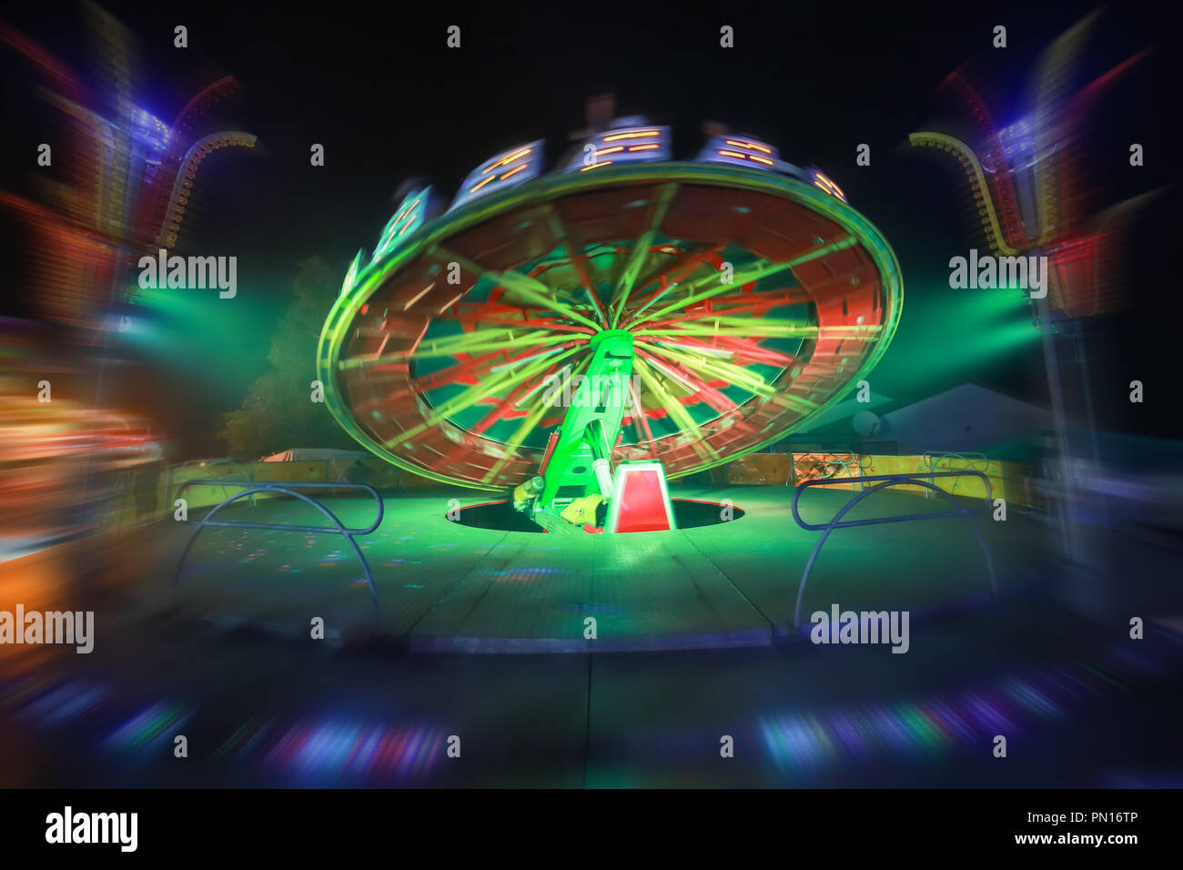 An illuminated rotating circular device in an amusement park with zoom ...