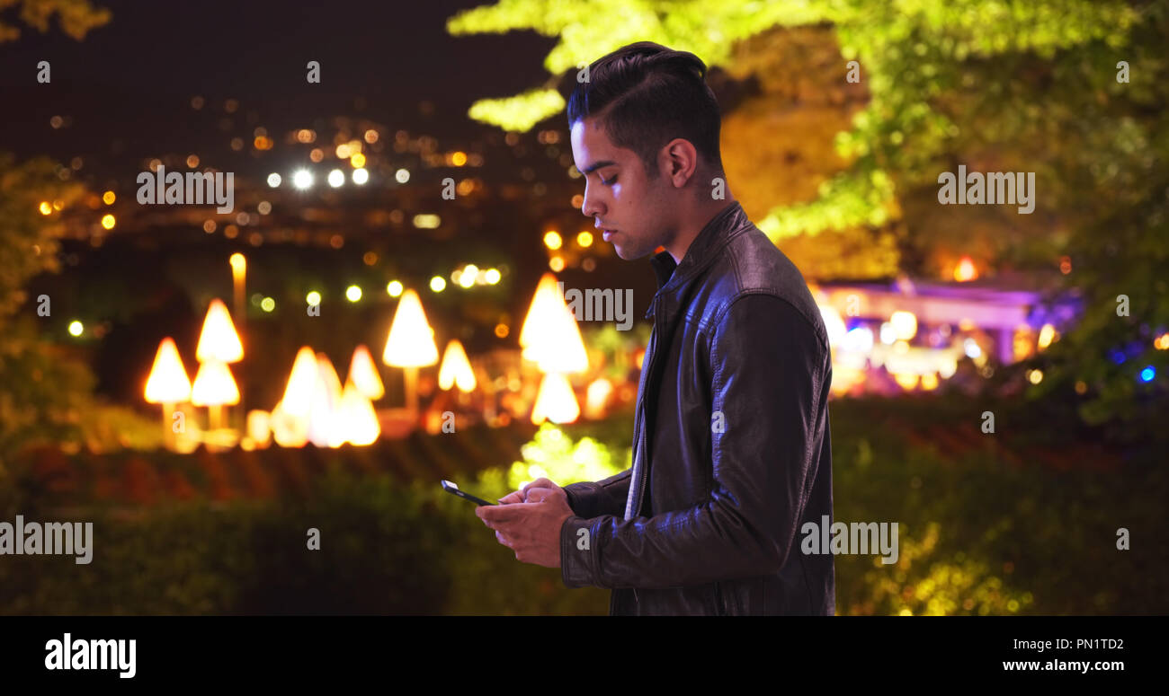 Millennial Latin man text messaging outside at night with view of city ...