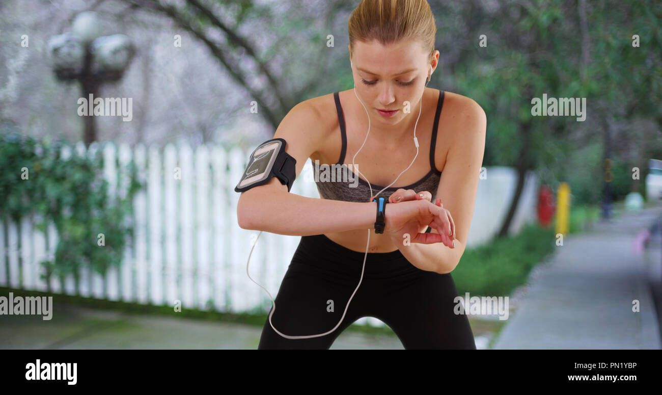 Woman runner using smartwatch fitness tracker while running on suburban ...