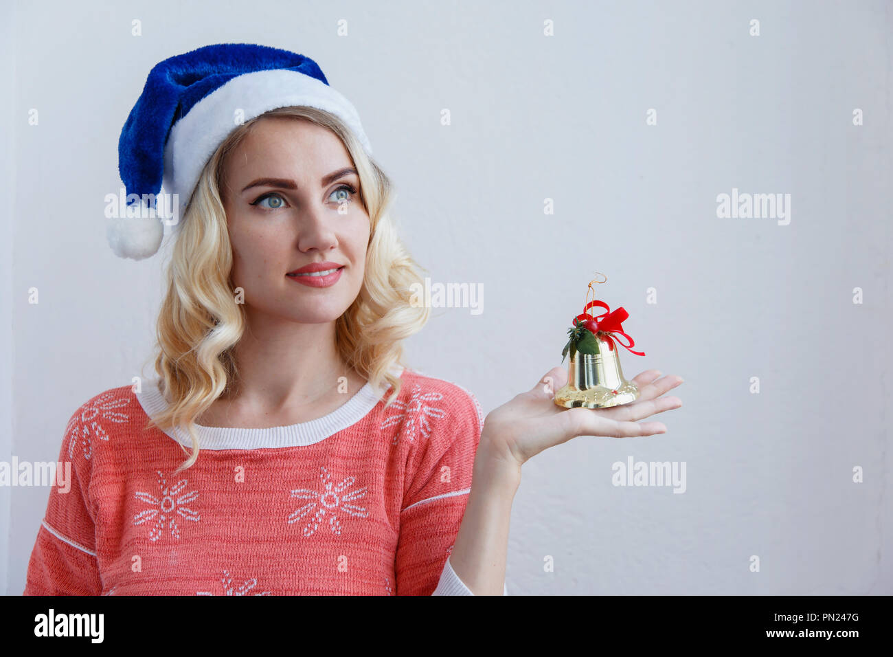 blond girl in a New Year hat with a bell in hands on a light background ...