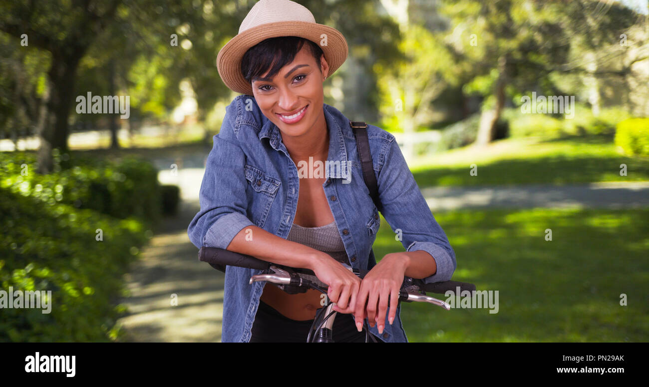 Happy smiling black woman leaning against handlebars on bike in park ...