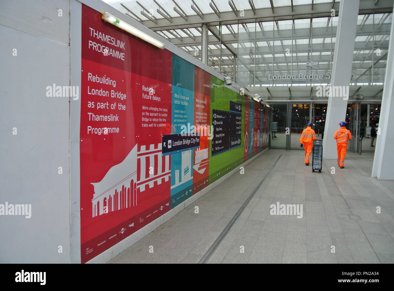 Two unidentifiable Network Rail workmen walking past a poster board ...