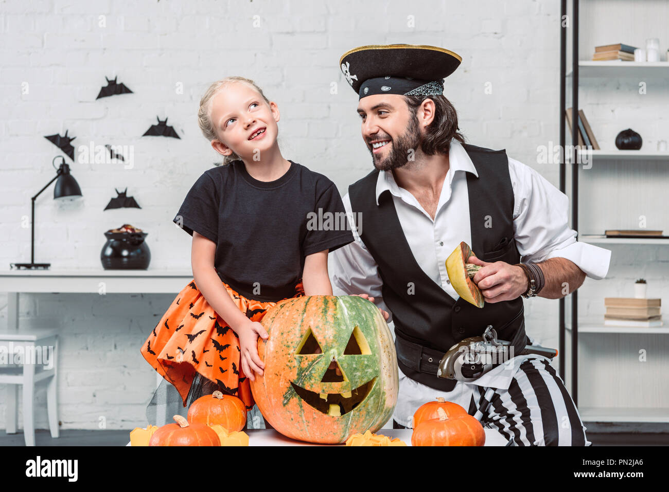 smiling father and daughter in halloween costumes at table with pumpkin ...
