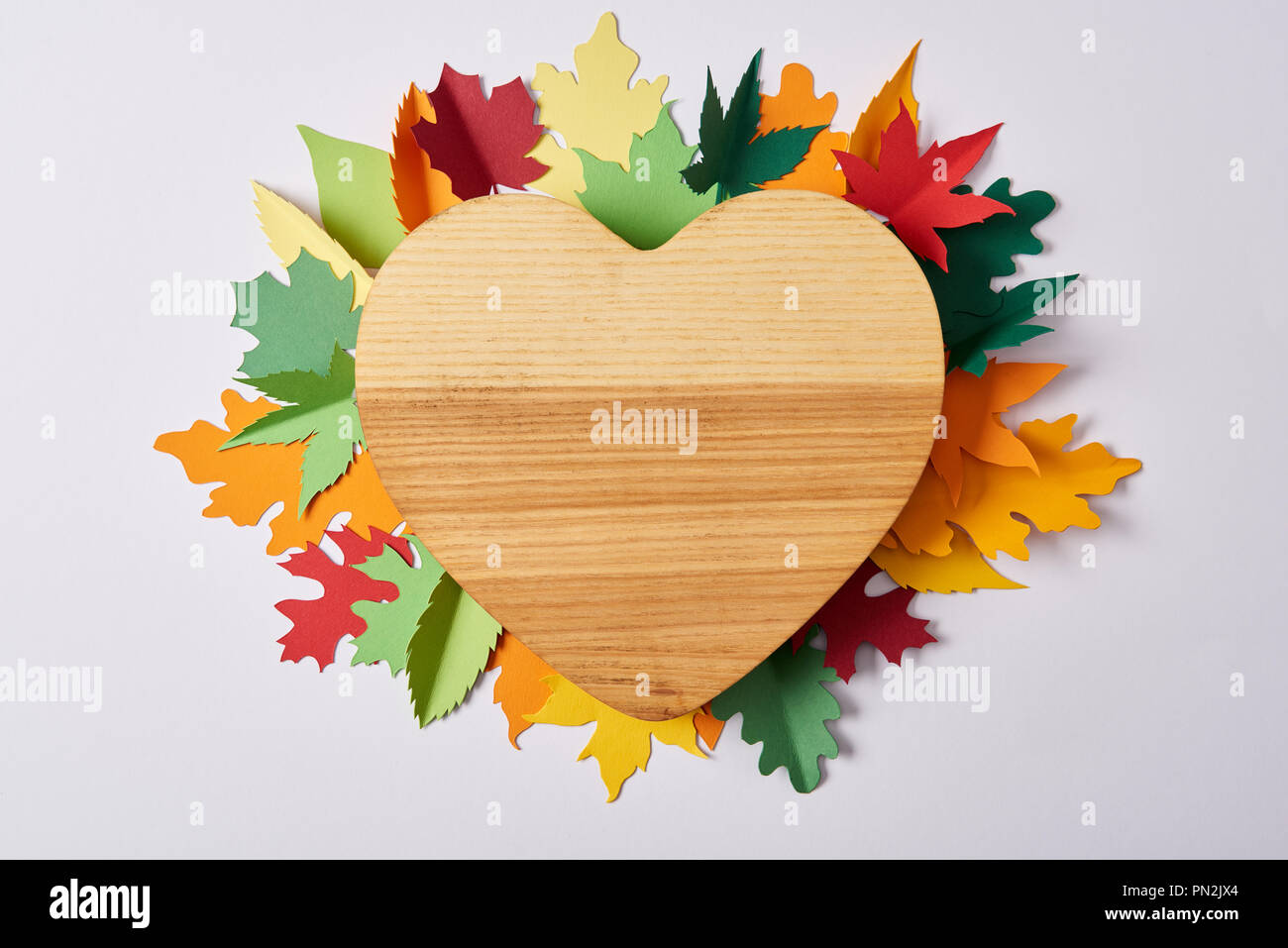 top view of wooden heart shaped board and colorful handcrafted leaves ...
